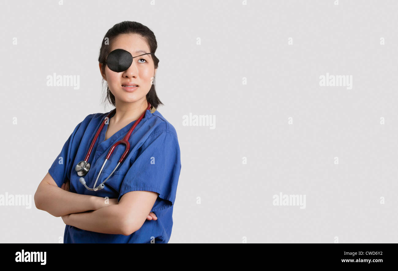 Asian female doctor wearing an eye patch looking up with arms crossed ...