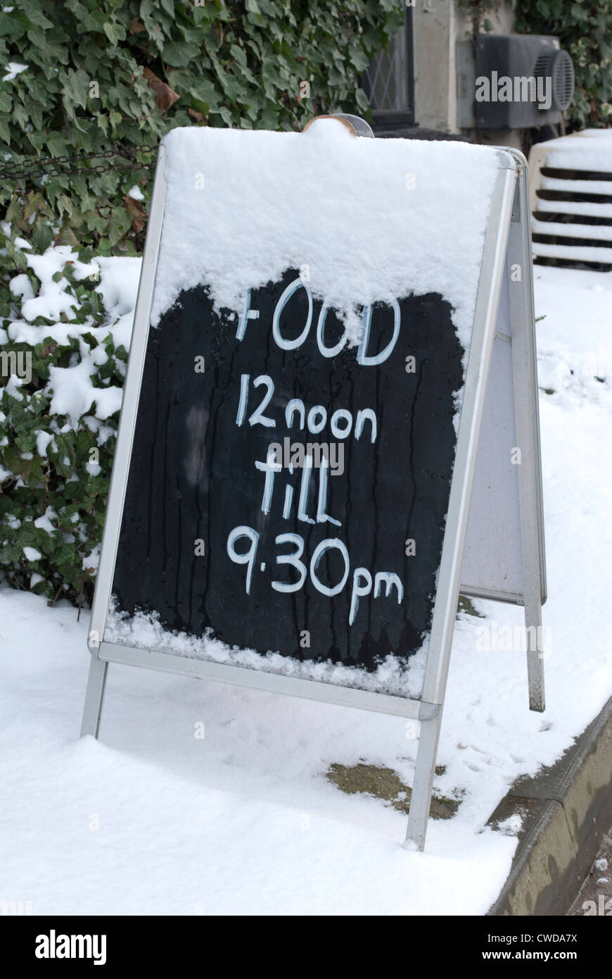 Snow covered sign board with 'Food 12 noon till 9.30pm' chalked on it ...
