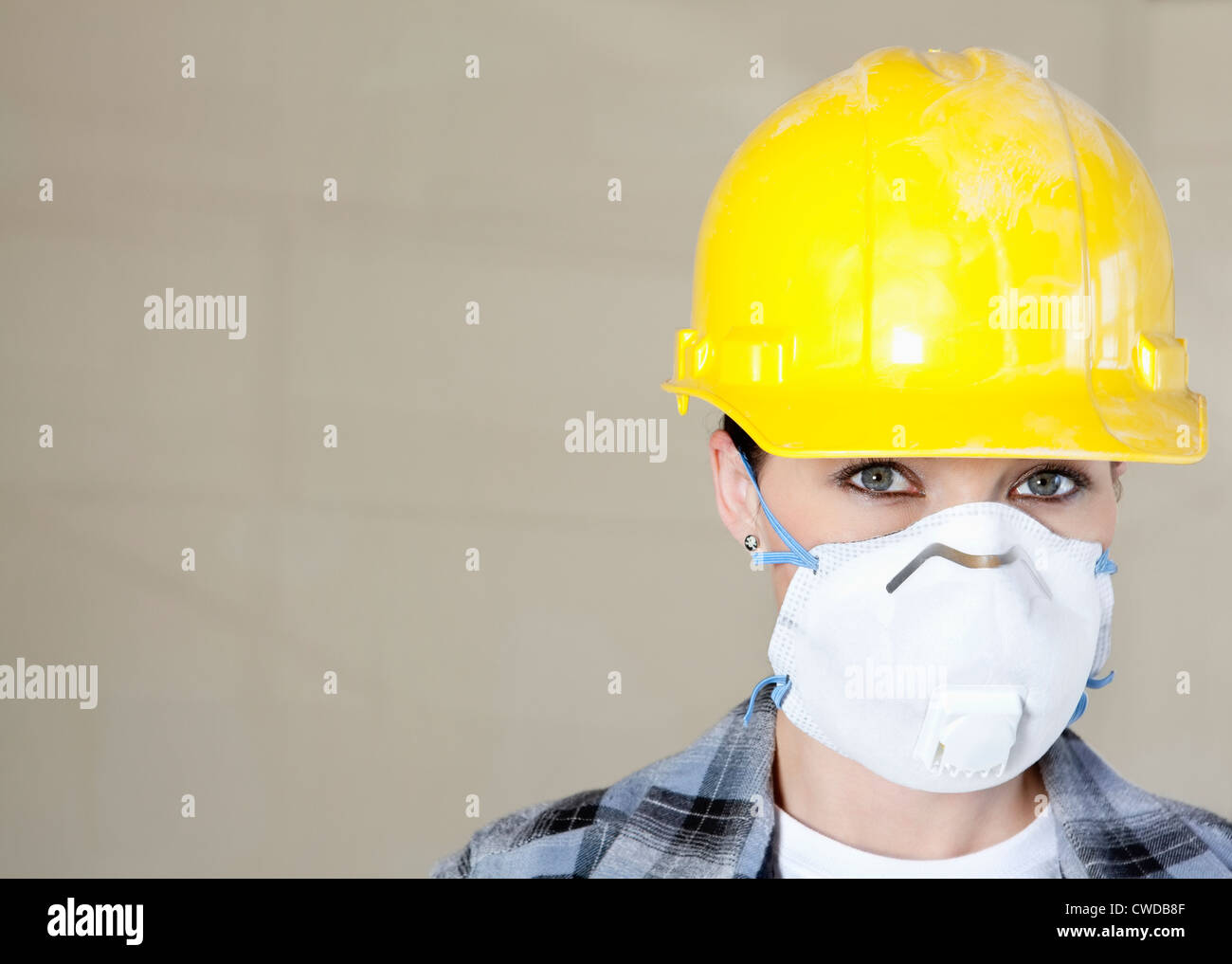 Portrait of female worker wearing dust mask and hardhat over colored ...