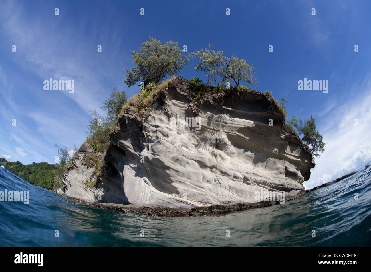 A dramatic island made up of what looks like sandstone overhangs a set ...