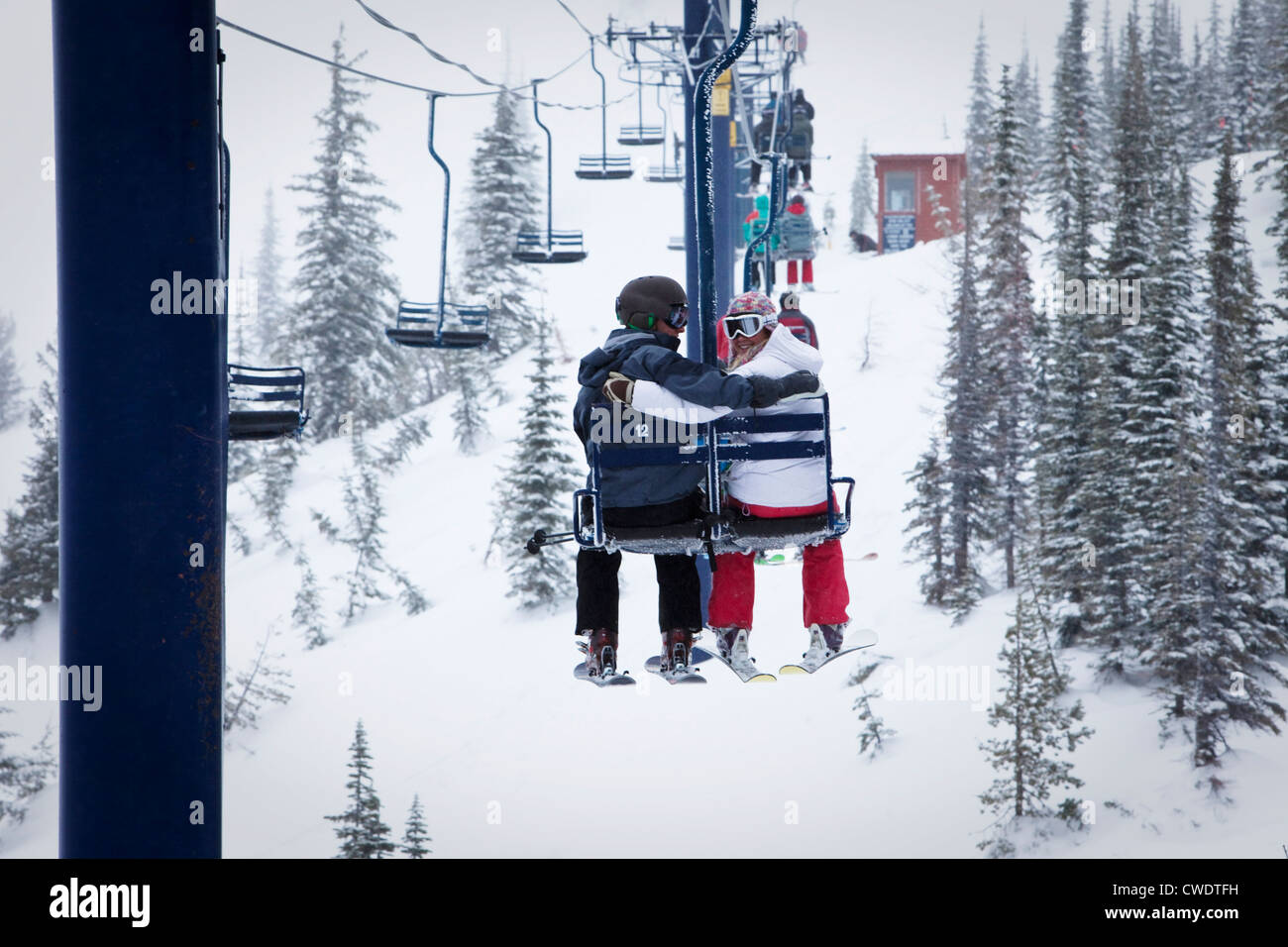 Two young adults smile while sitting on a double chairlift at a ski ...