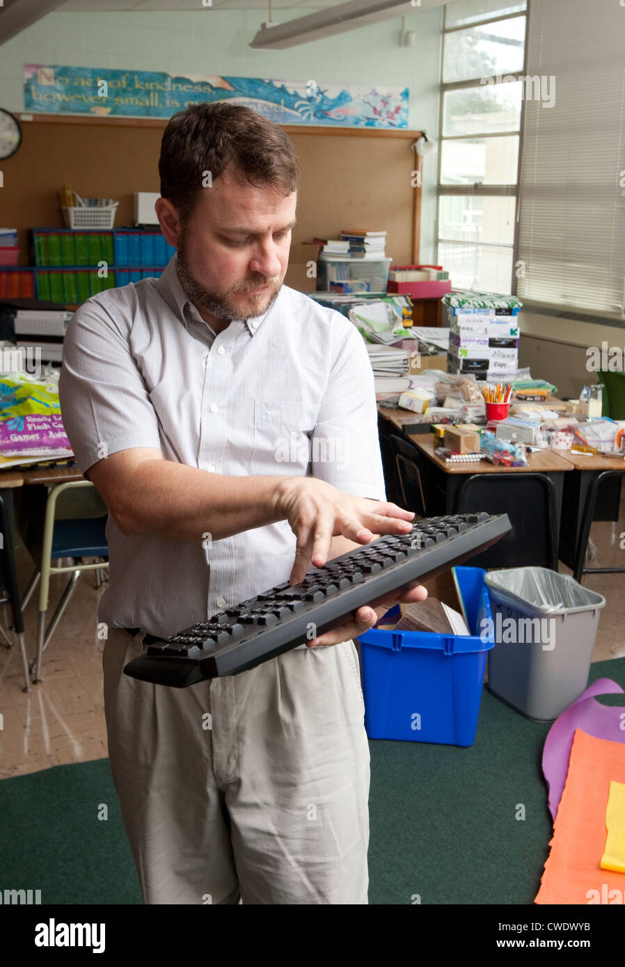 Young male elementary school teacher holds up, uses keyboard to use ...