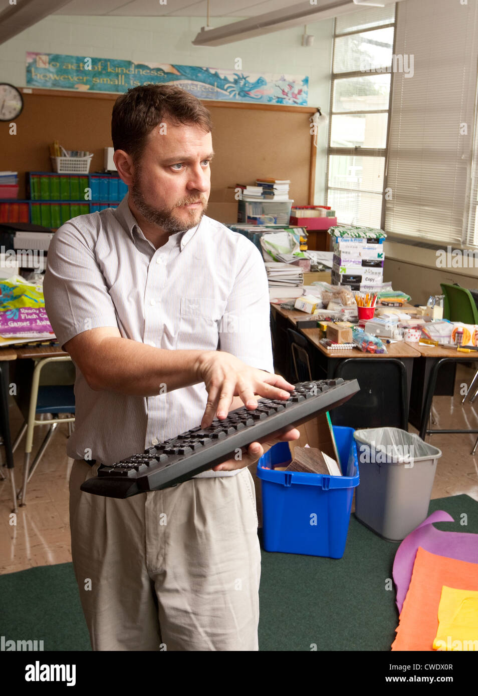 Young male elementary school teacher holds up, uses keyboard to use ...