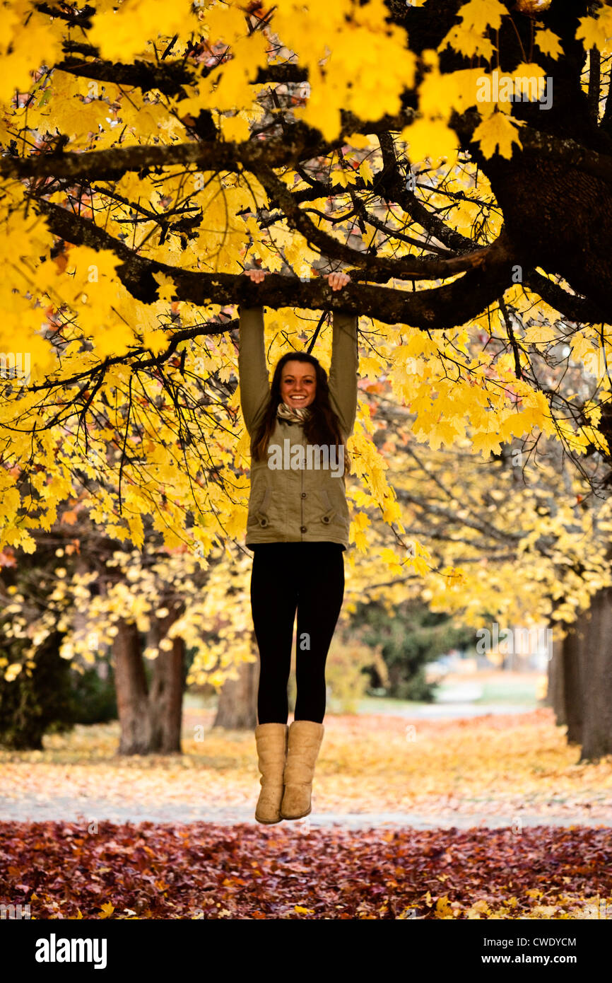 A beautiful young woman smiles while hanging from a tree in the peak ...