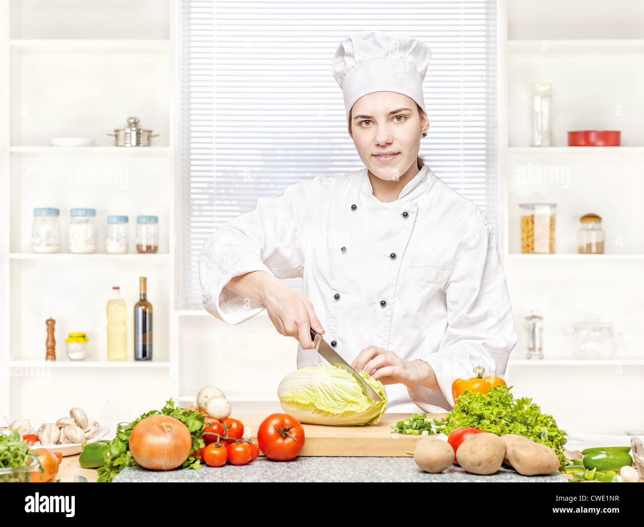 Young female chef cutting cabbage on the cutting board in kitchen Stock ...