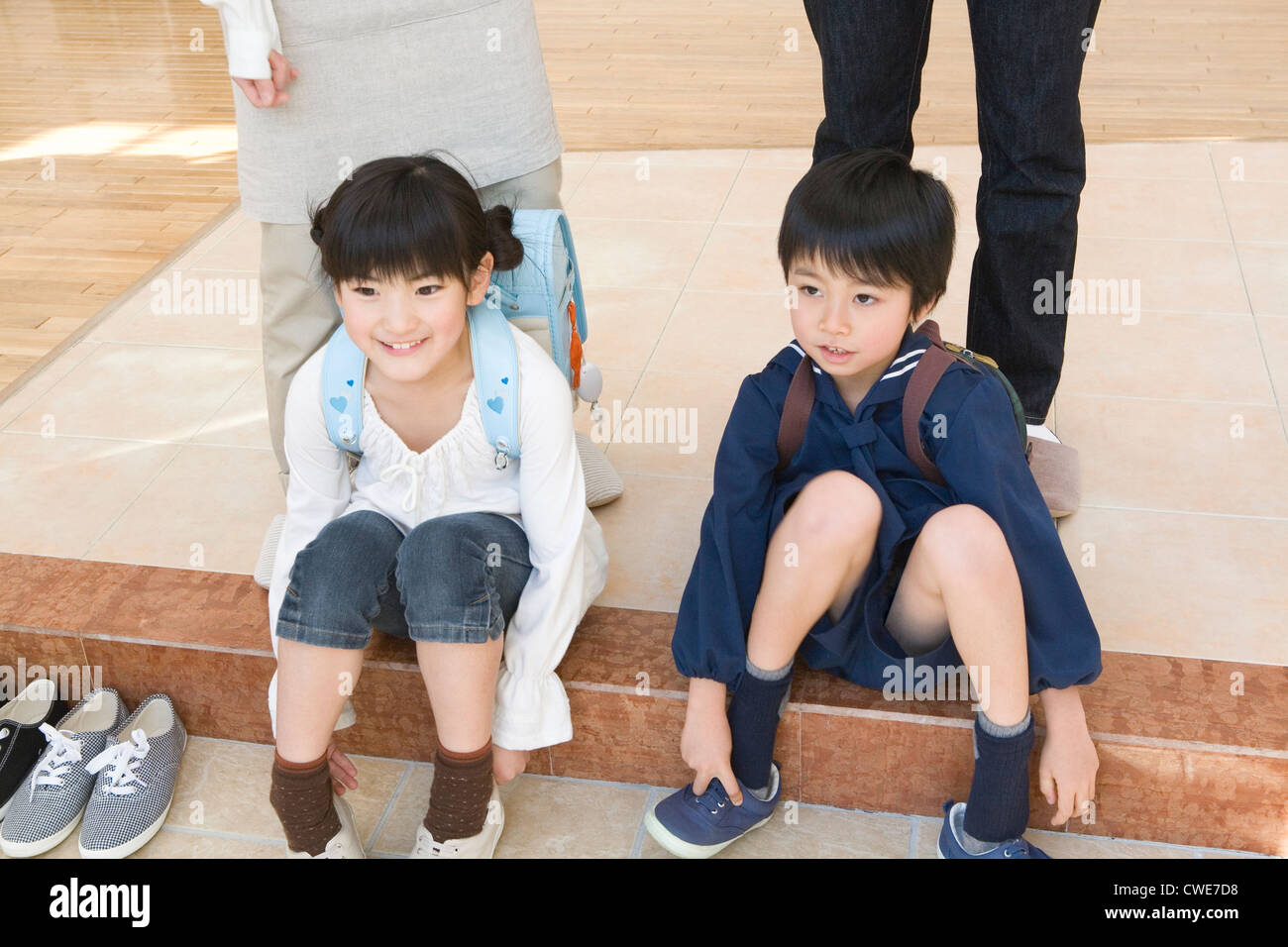 Two children sitting and putting on shoes at entrance Stock Photo - Alamy