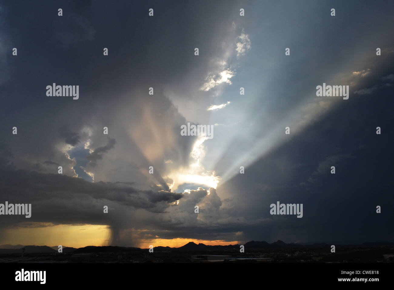 Light rays shine through clouds as rain pours in the distance Stock ...