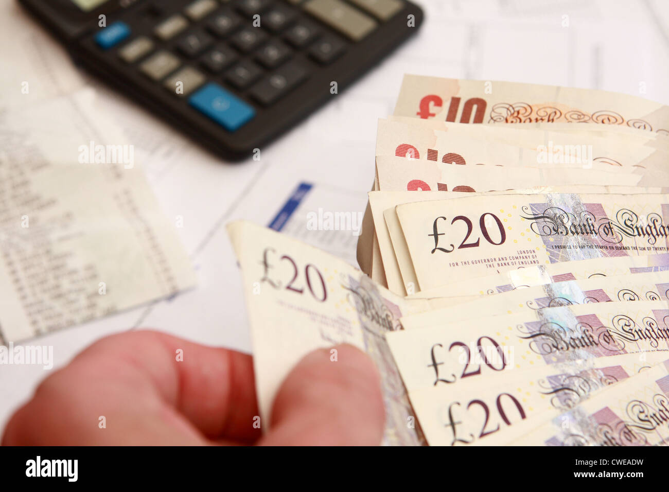a hand pulling a £20 note from a bundle of notes with a calculator and ...