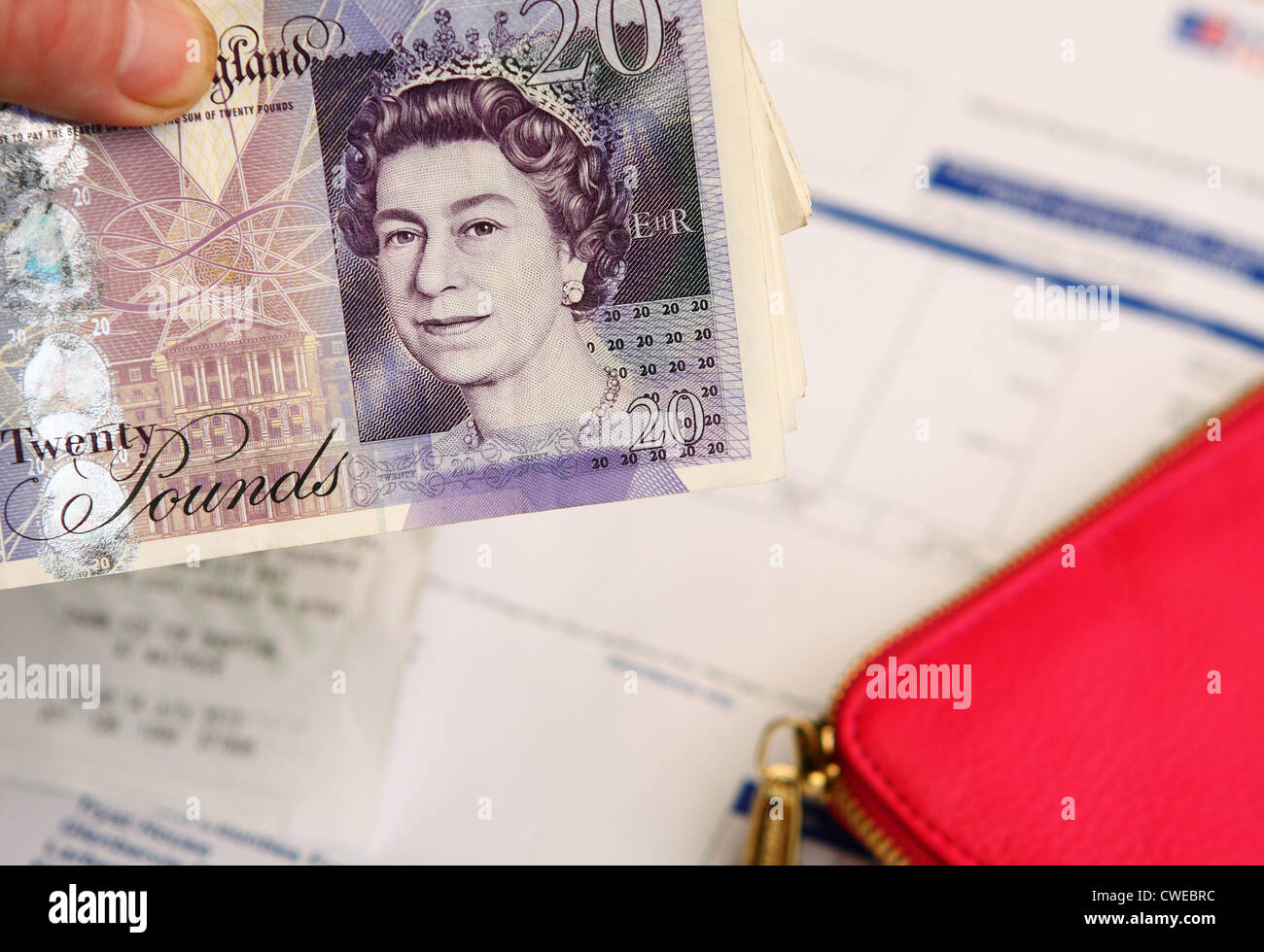 the thumb of a hand holding a £20 note with a purse and out of focus ...