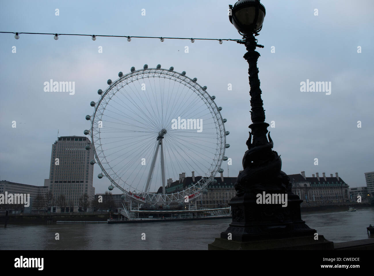 The London Eye silhouetted against a dull grey sky with a fancy street ...