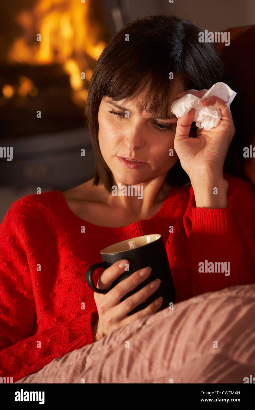 Sick Woman With Cold Resting On Sofa By Cosy Log Fire Stock Photo - Alamy