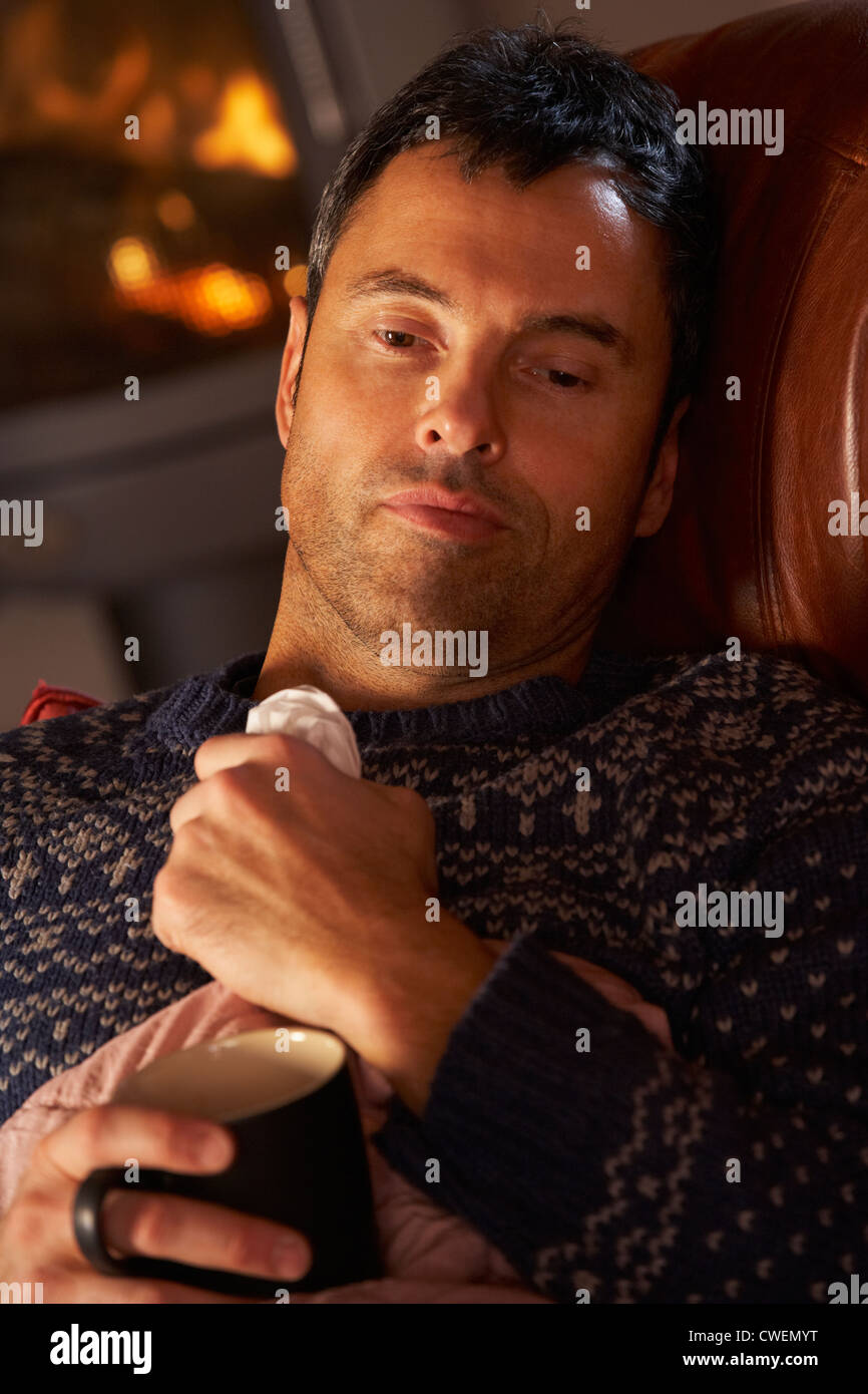 Sick Man With Cold Resting On Sofa By Cosy Log Fire Stock Photo - Alamy