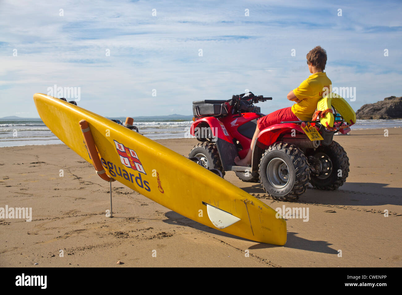 Lifeguard with surfboard on quadbike surveying sandy beach at low tide ...