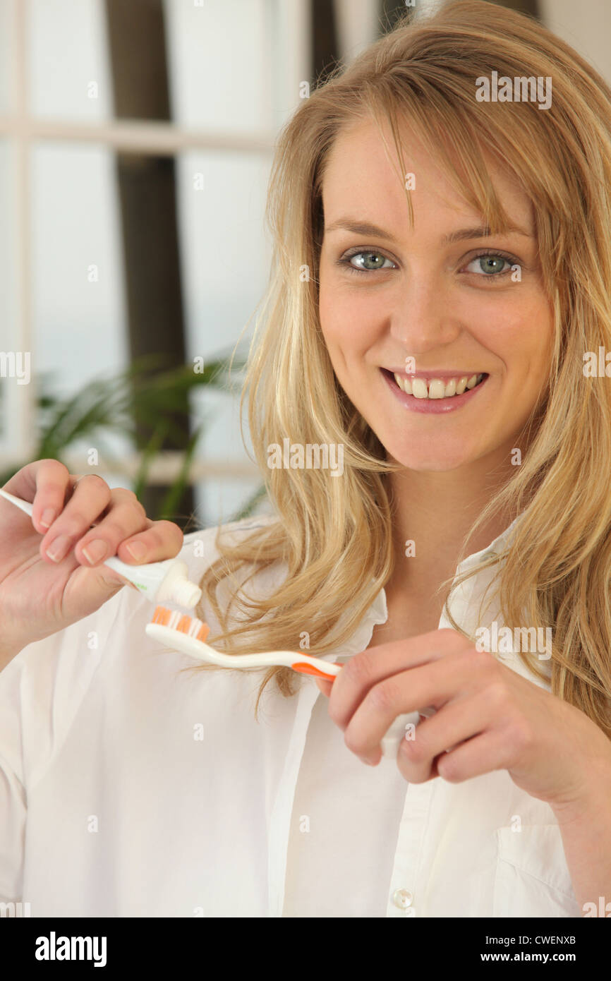 a blonde woman putting toothpaste on her toothbrush Stock Photo - Alamy