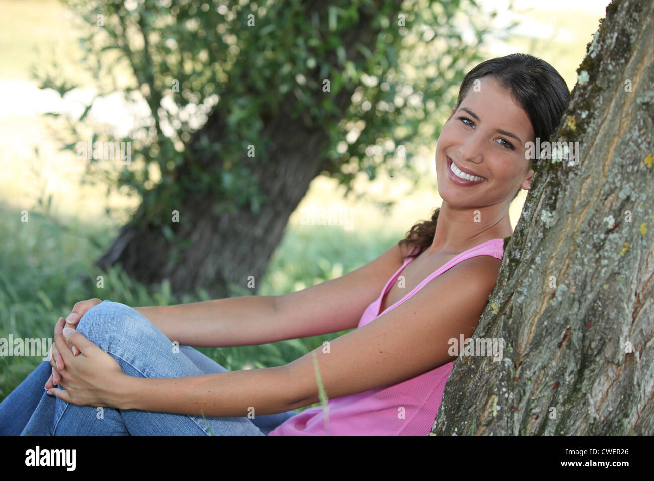 Woman sat leaning against tree trunk Stock Photo - Alamy