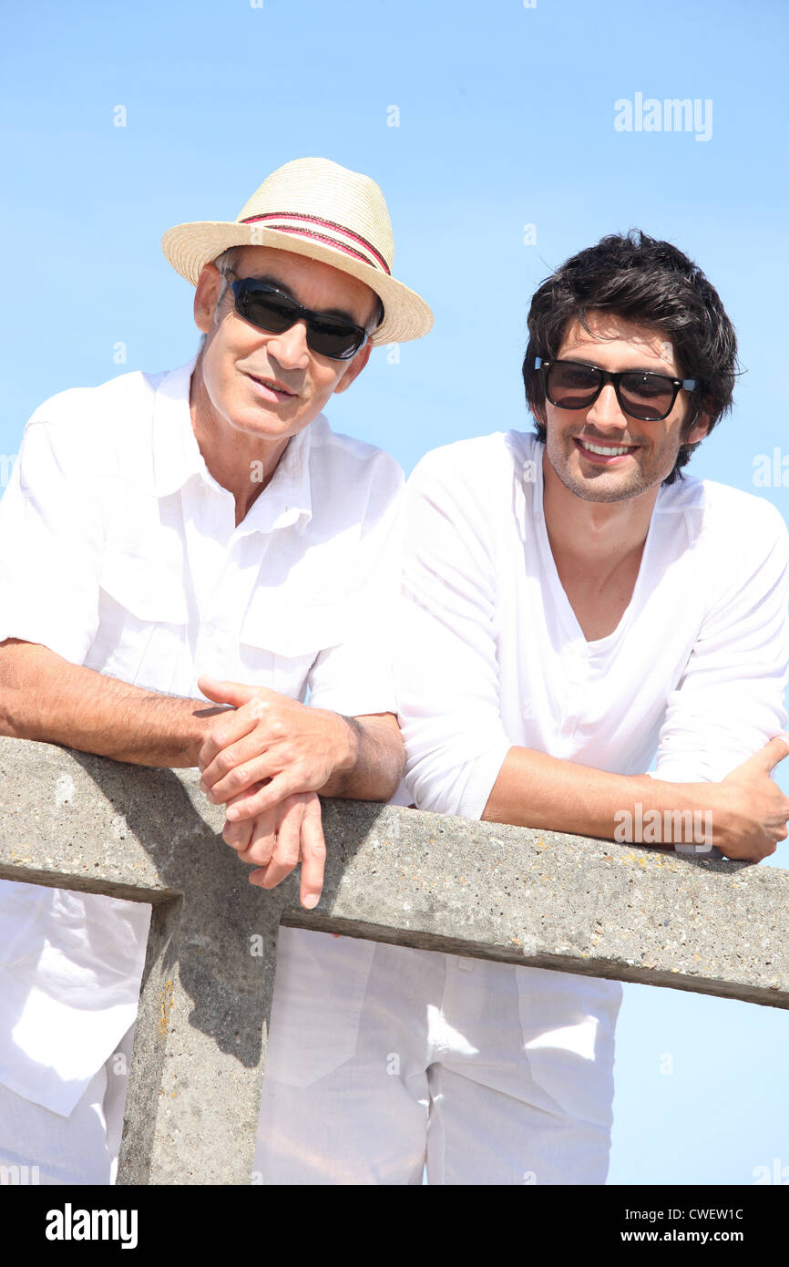 Two men in white leaning on a fence with a blue sky background Stock ...