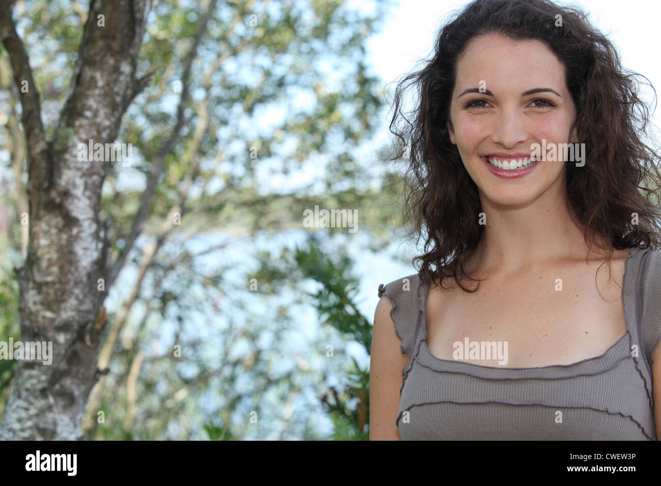 Smiling young woman standing next to a tree Stock Photo - Alamy