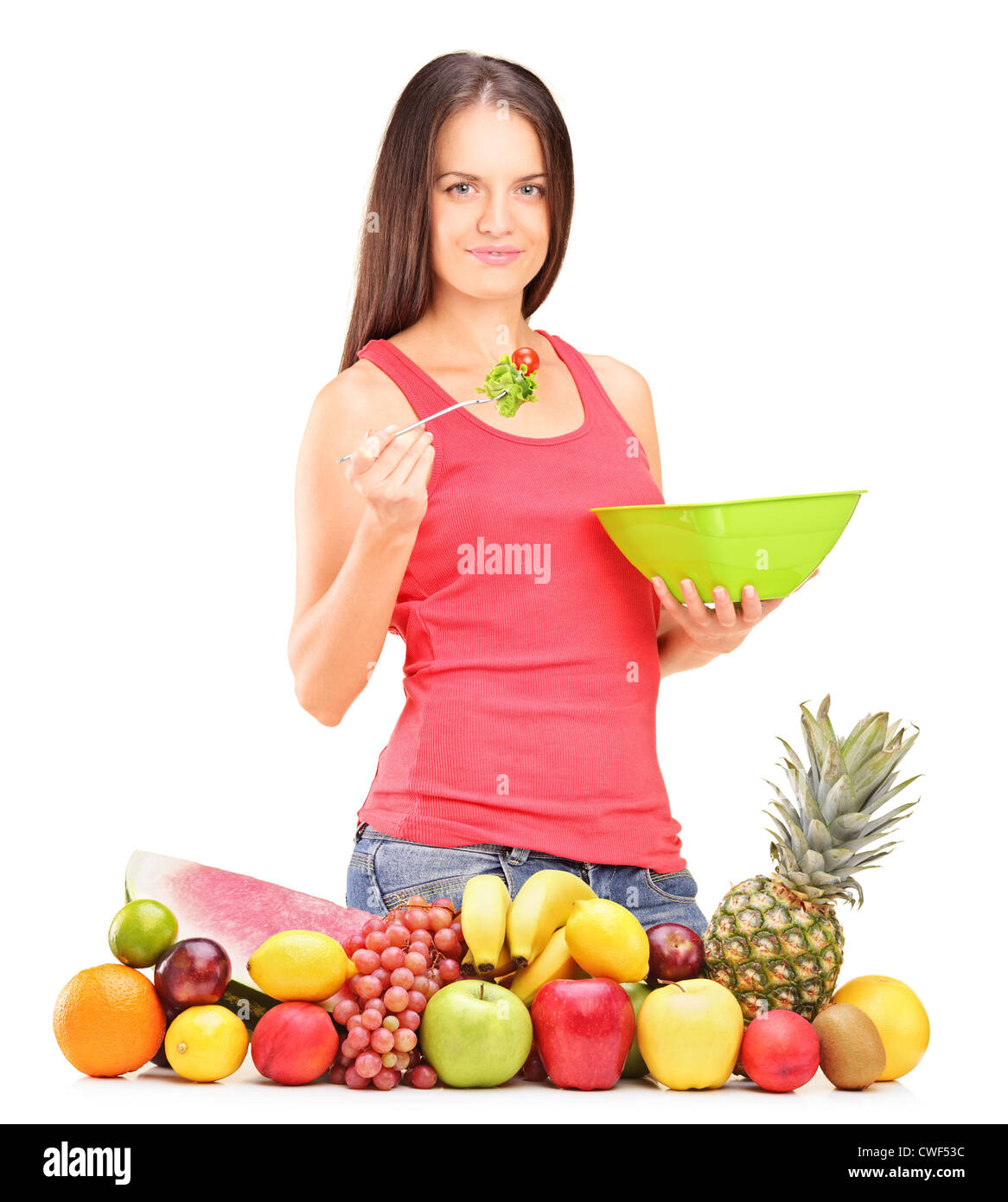 Young woman eating a salad standing behind a pile of fruits isolated on ...