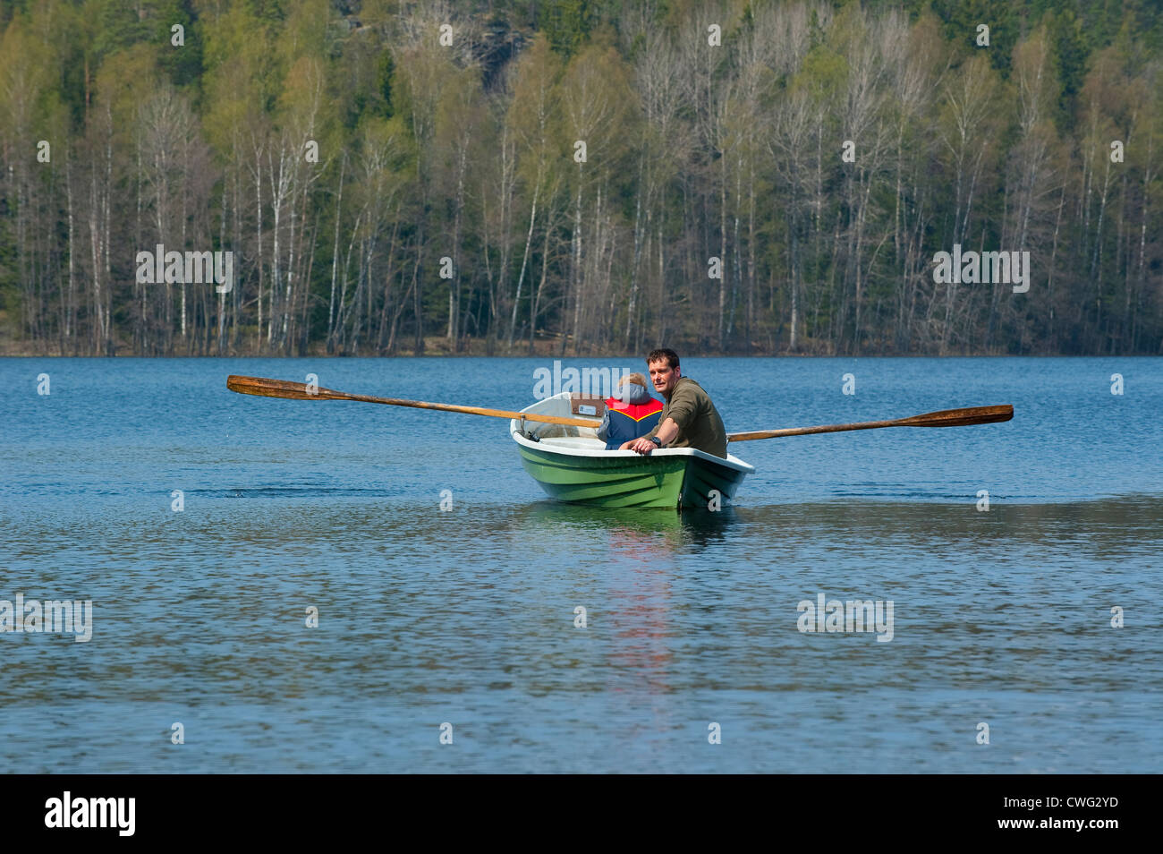 Young boy rowing a boat on a lake with his father watching him Stock ...