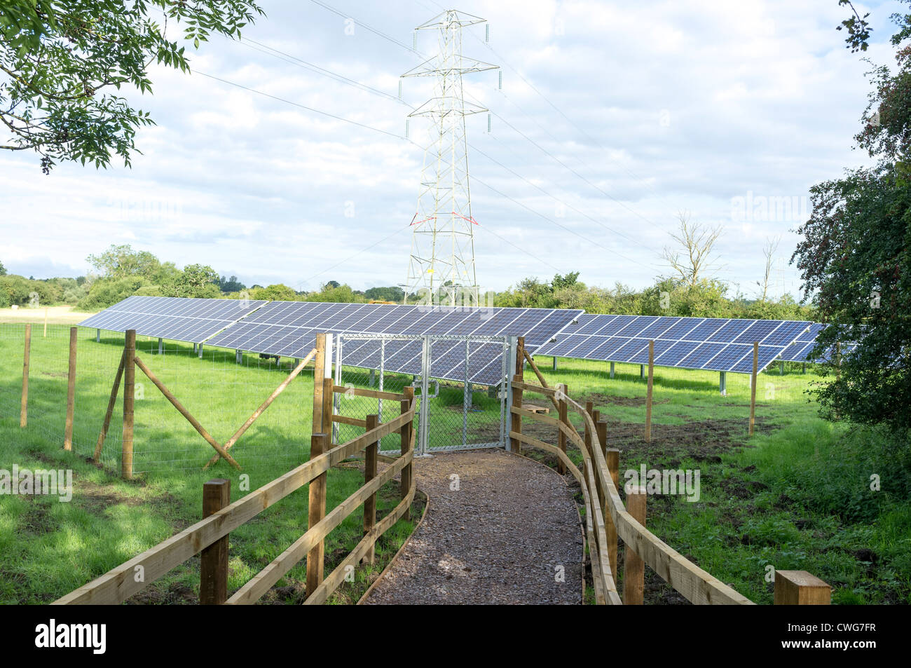 Solar panels in a field behind locked gates with electricity pylon in ...