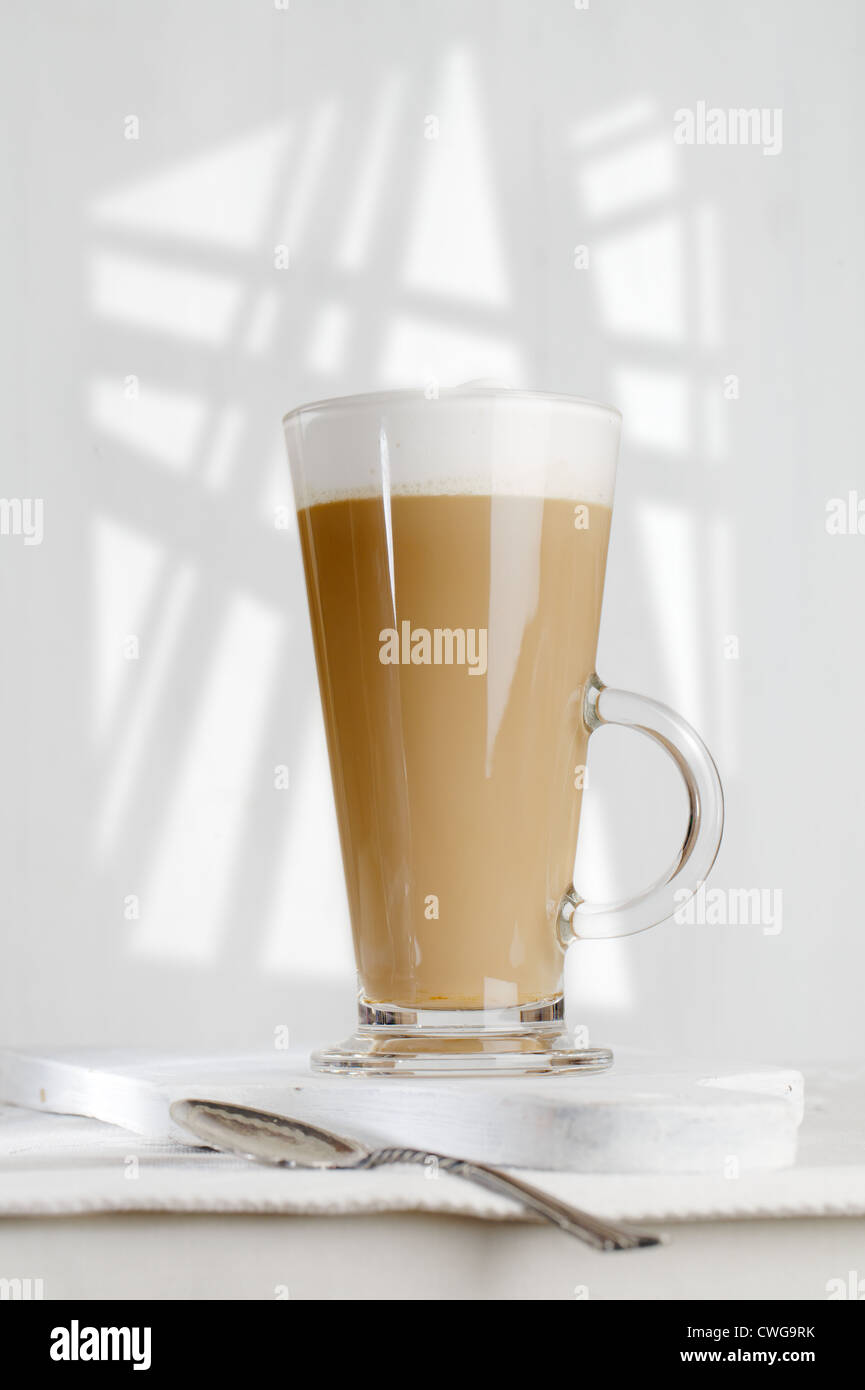 coffee latte with frothy milk in tall glass, gobo light, white wood ...