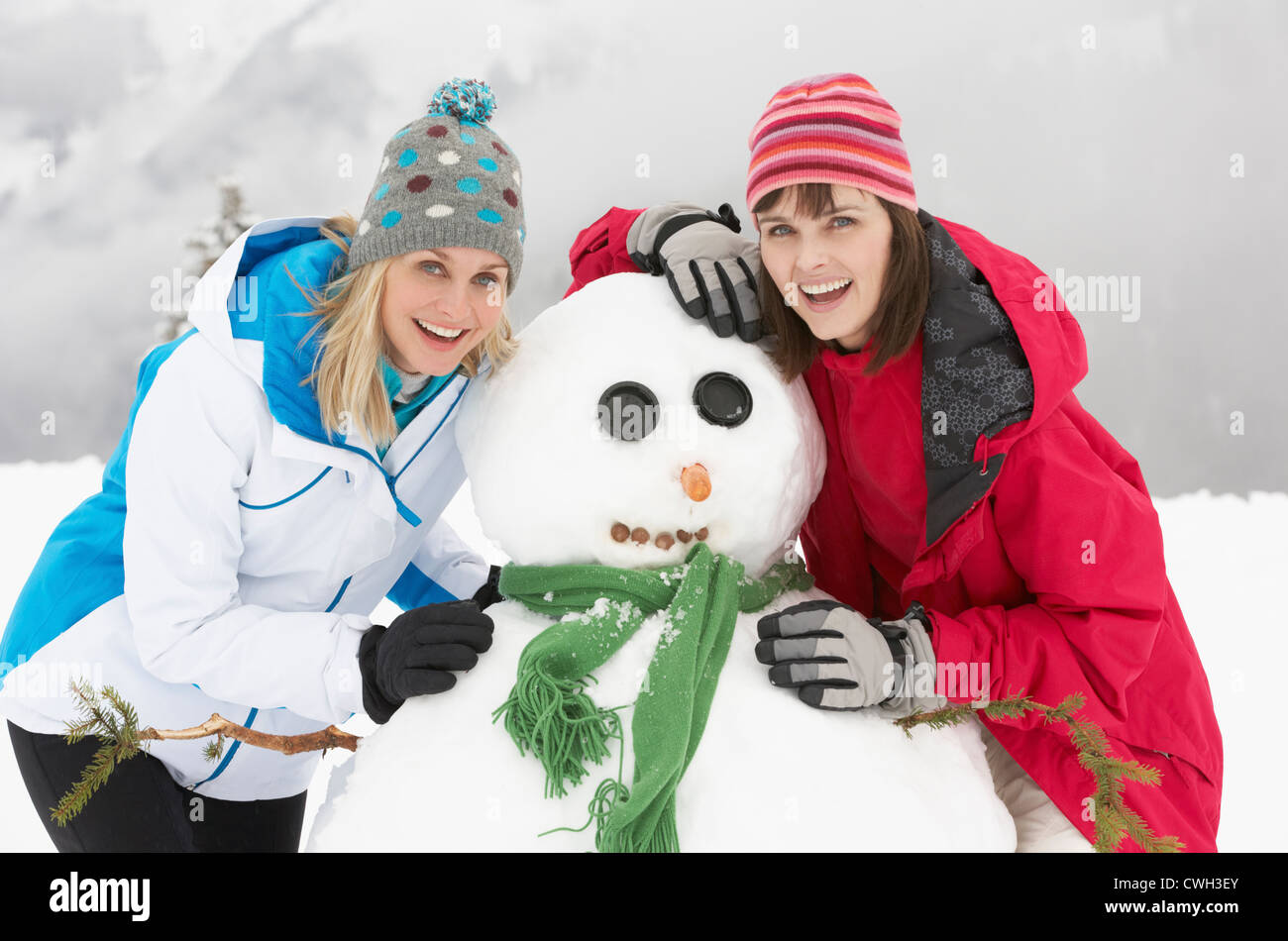Two Female Friends Building Snowman On Ski Holiday In Mountains Stock ...