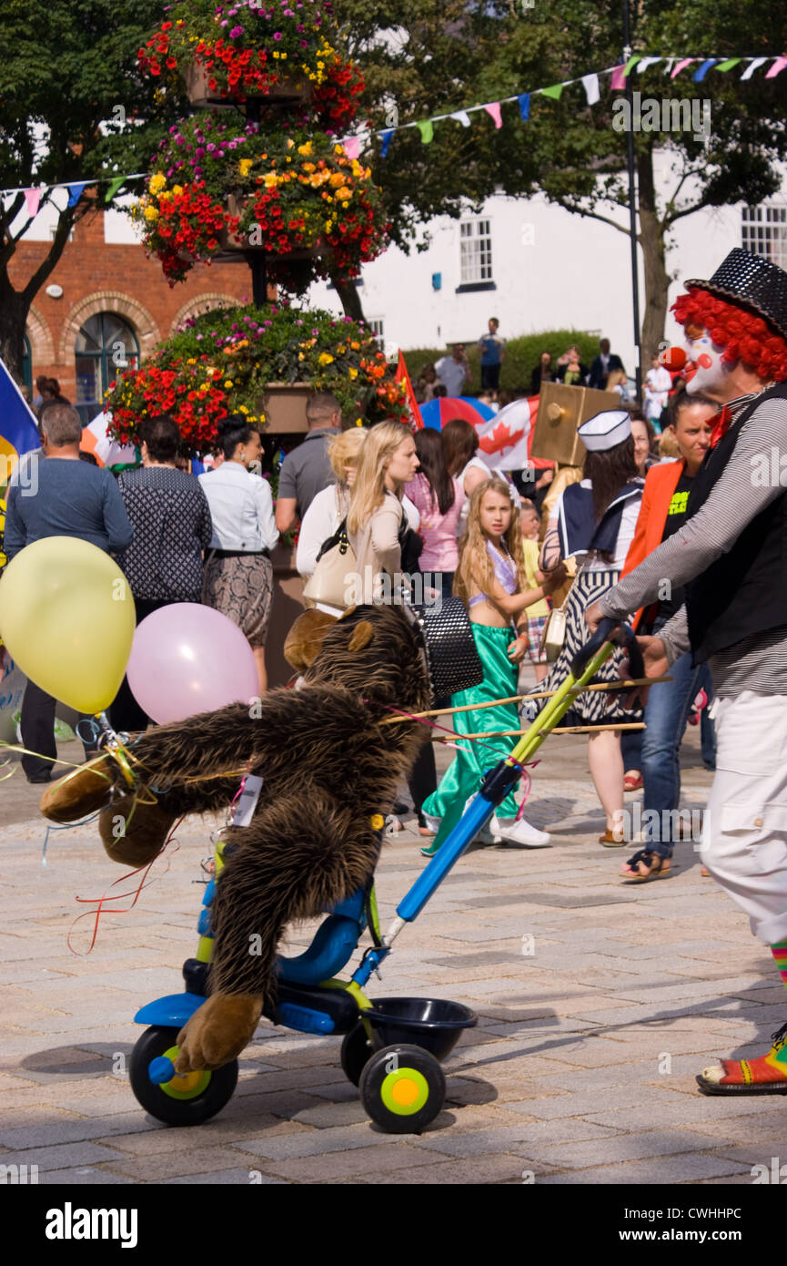 A STUFFED MONKEY BEING PUSHED IN A PUSHCHAIR BY A CLOWN IN FANCY DRESS ...