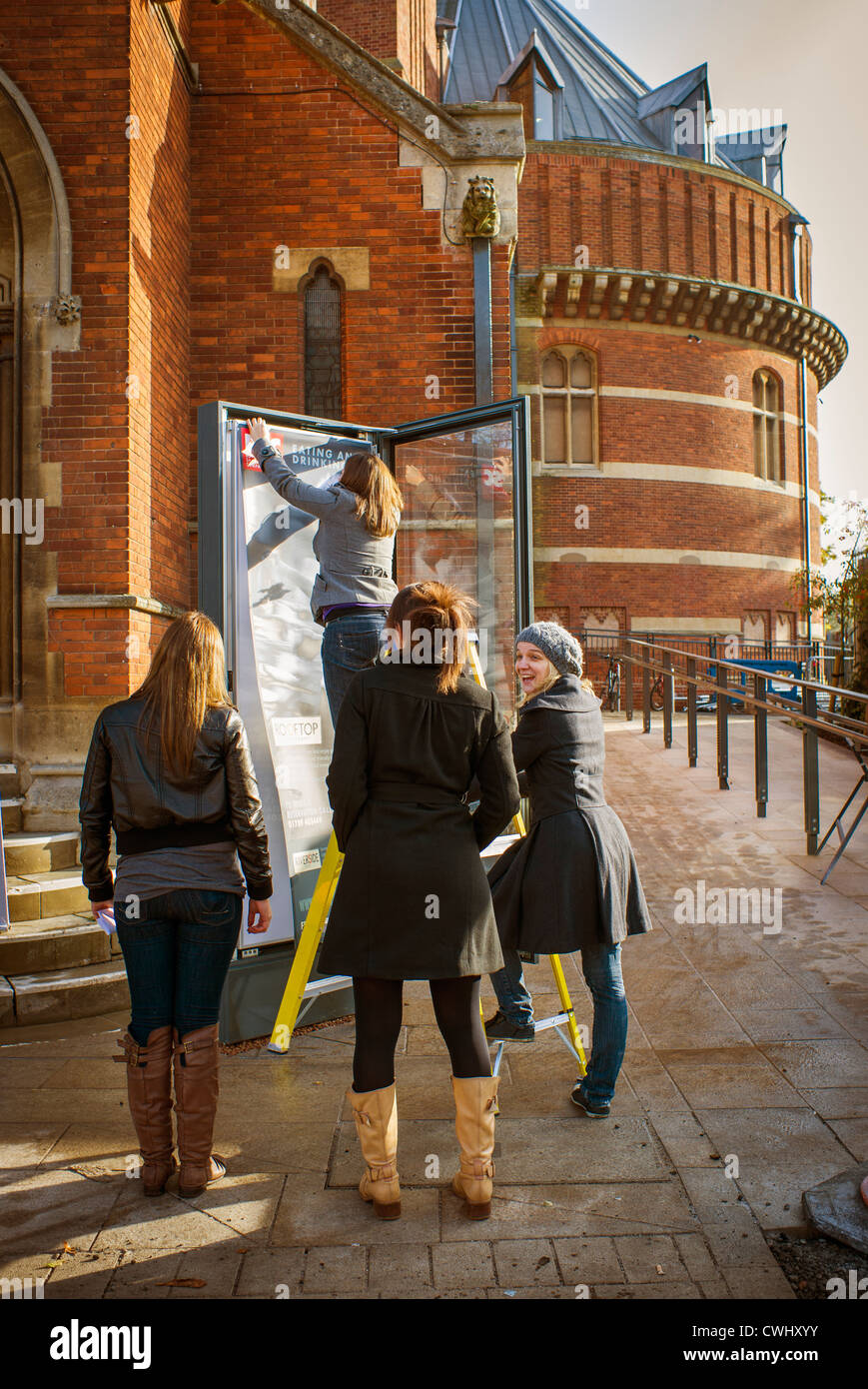 Four young females fixing promotional posters. One with jocular smiling ...