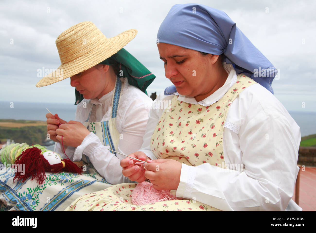 Two azorean women making handicraft outdoors while wearing traditional ...
