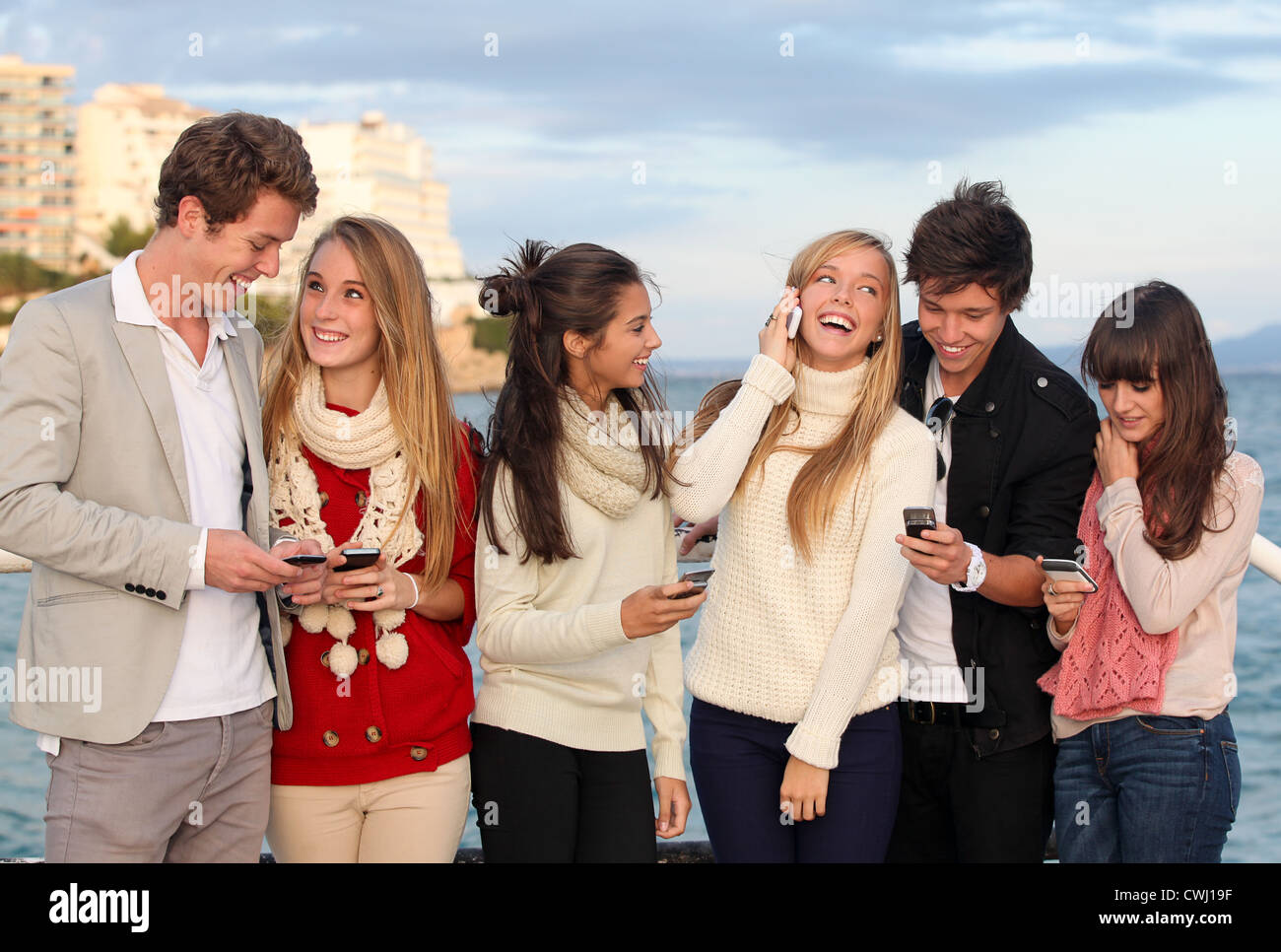group of happy smiling teens, kids, texting and calling with mobile or ...