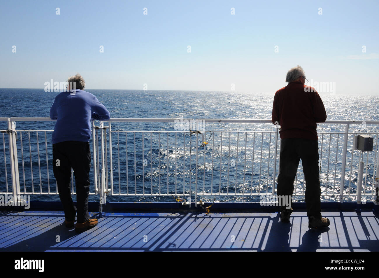 Two elderly, senior, men, wearing sweaters, leaning on handrail looking ...