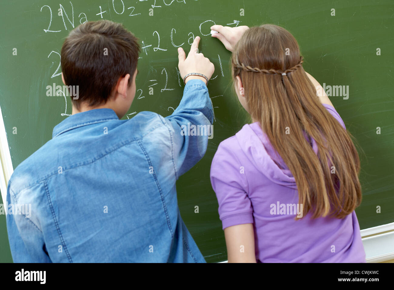 Back view of guy pointing at blackboard while explaining formula to ...