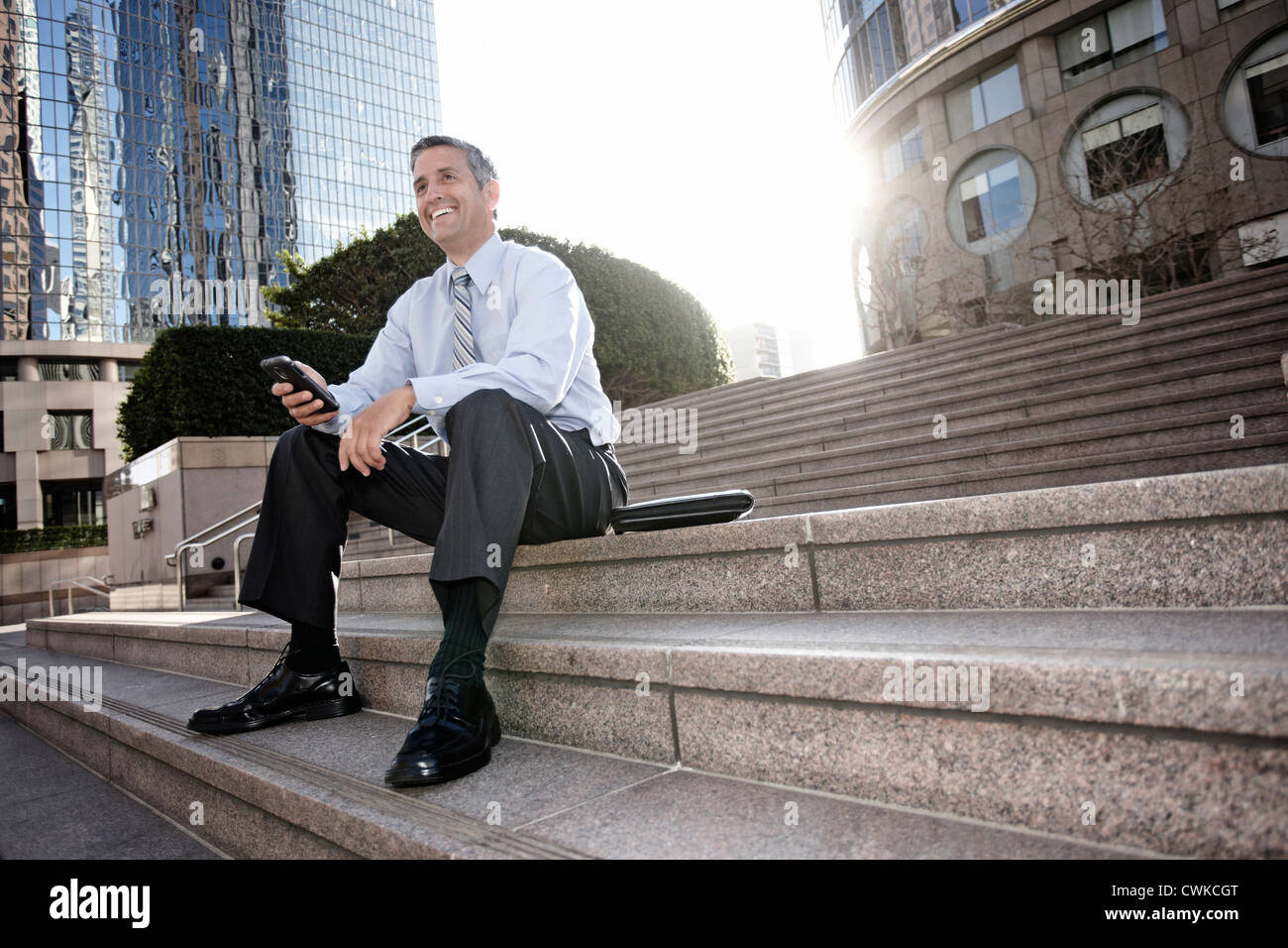 Hispanic businessman sitting on steps holding cell phone Stock Photo ...