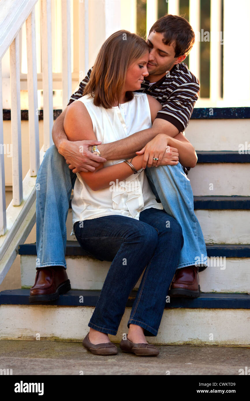A young couple in love share a romantic embrace while sitting on steps ...