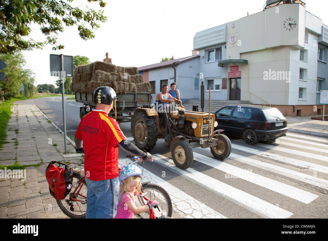 Polish farm family bringing load of hay into town while bicyclists wait ...