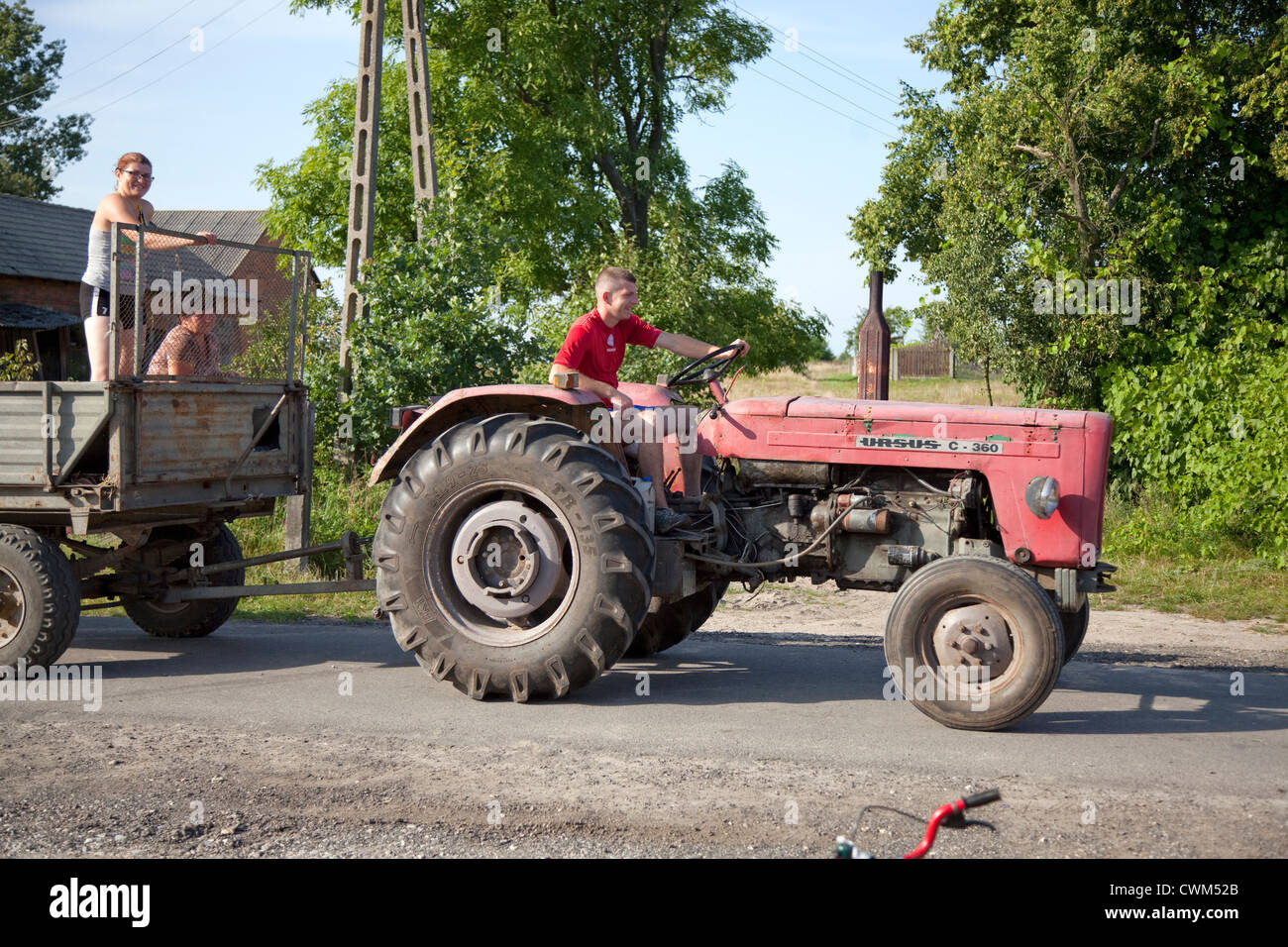 Polish man driving tractor and cart carrying two women along village ...