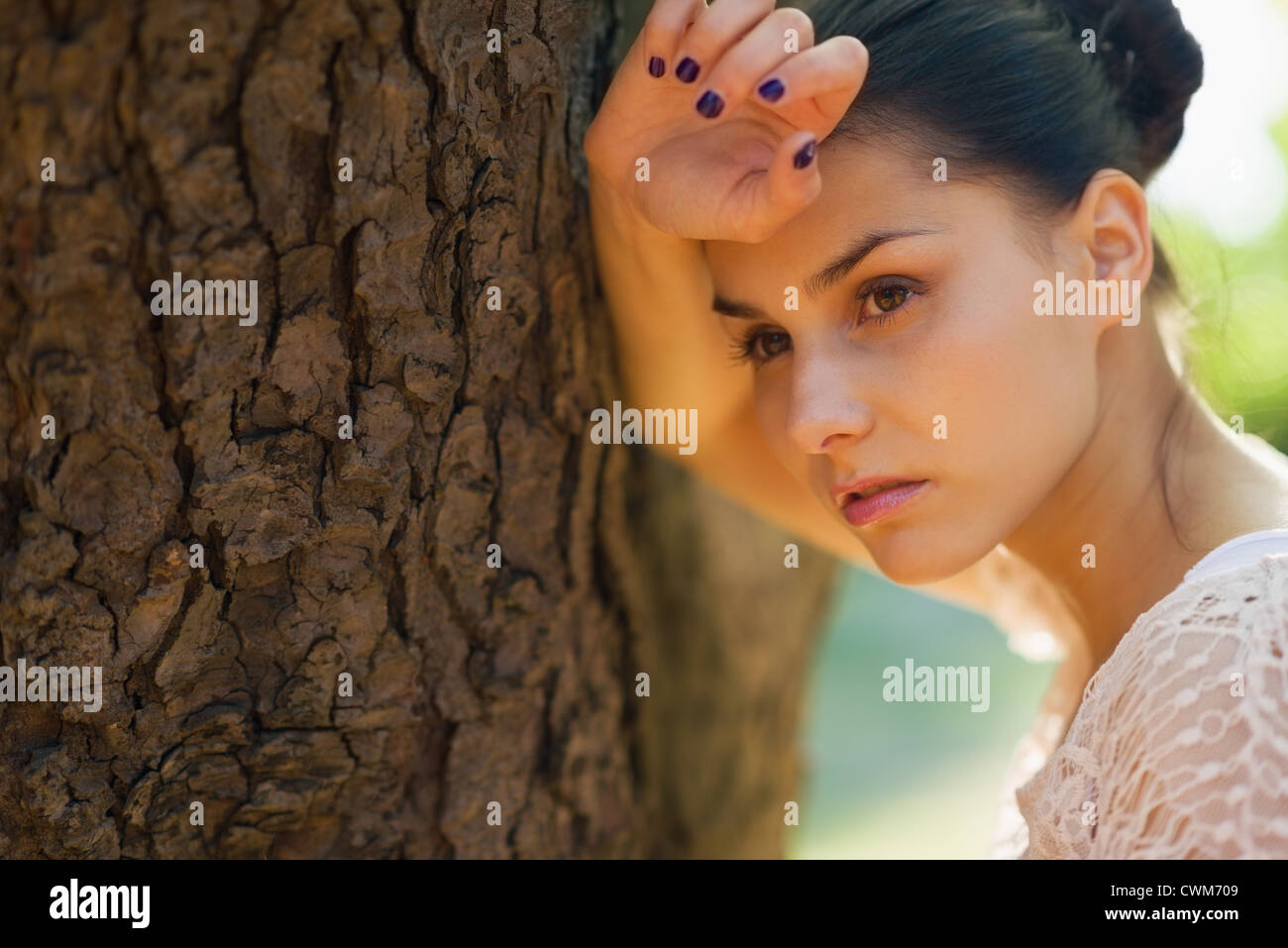 Thoughtful girl lean against tree Stock Photo - Alamy