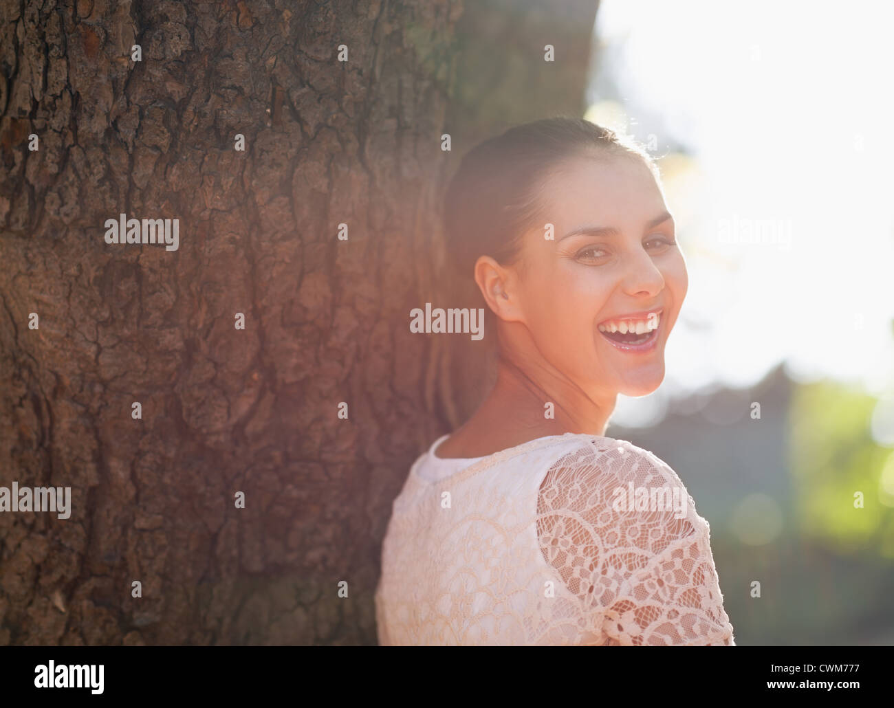 Laughing young woman lean against tree Stock Photo - Alamy