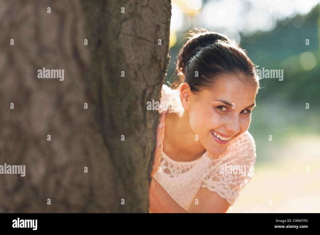 Smiling young woman looking out from tree Stock Photo - Alamy