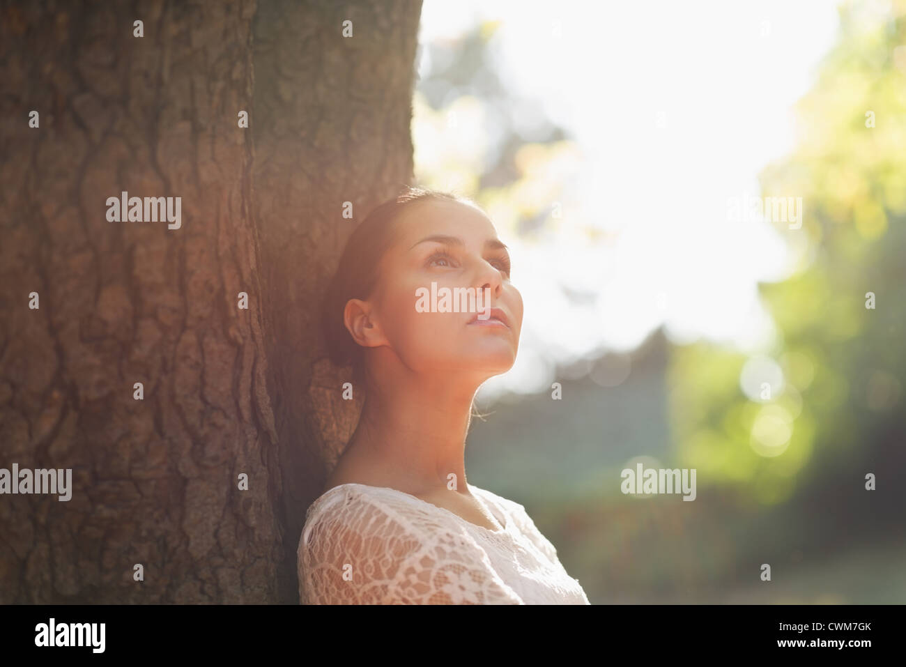Thoughtful young woman lean against tree Stock Photo - Alamy