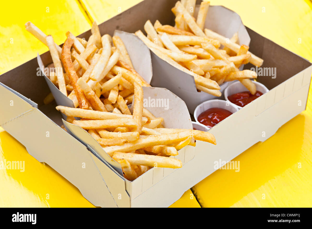 Portions of french fried potatoes with ketchup in cardboard take-out ...