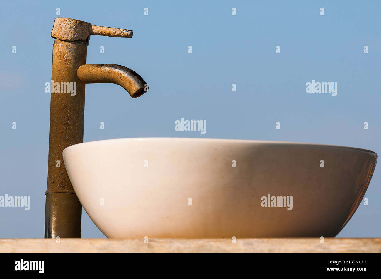 Washbasin and tap covered by limescale with blue sky on background ...