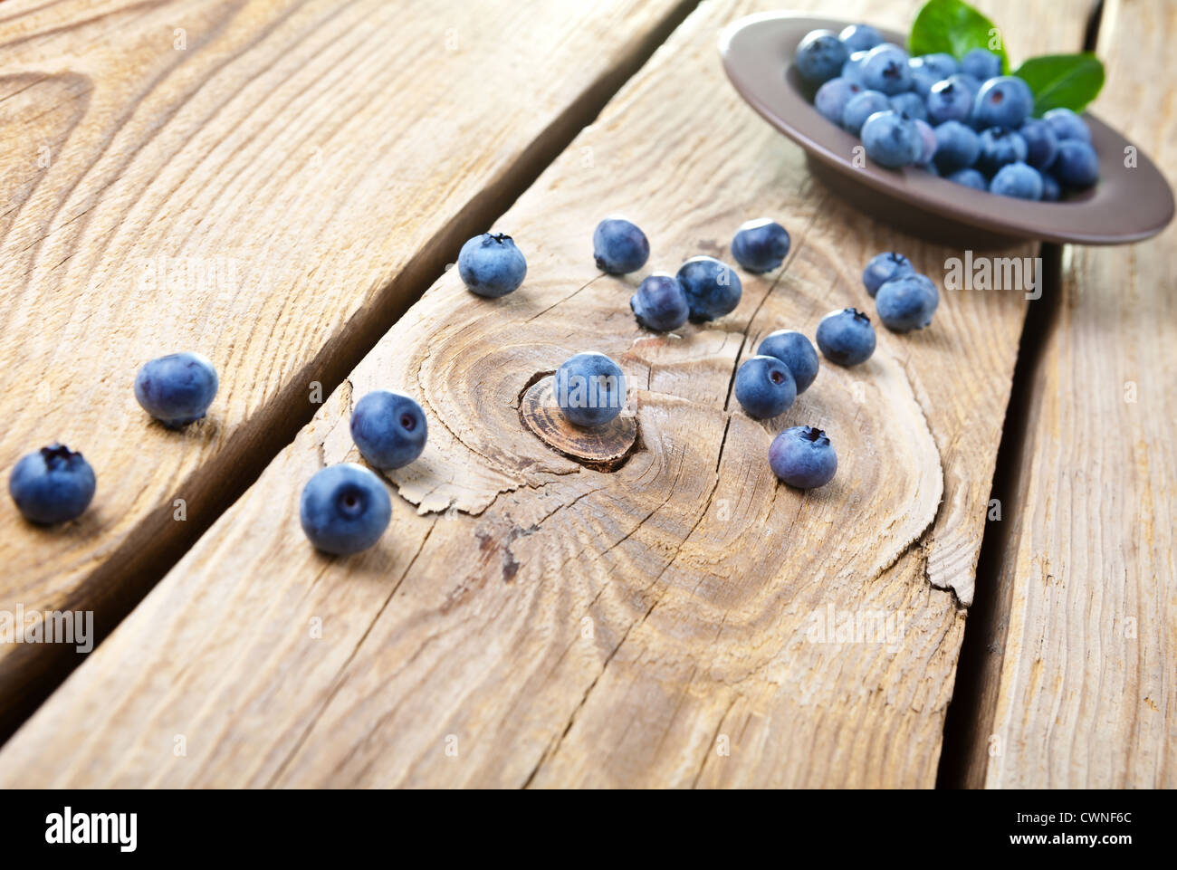 Fresh blueberries with leaves in brown bowl. Some blueberries spilled ...