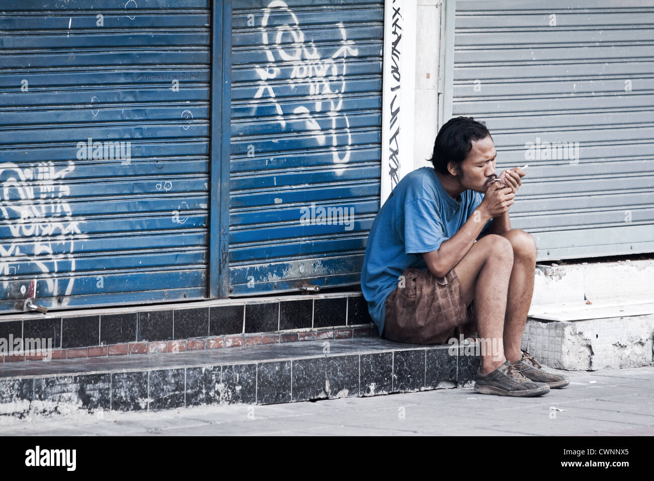 Man lighting cigarette sat outside a shop in Bangkok. street scene of ...
