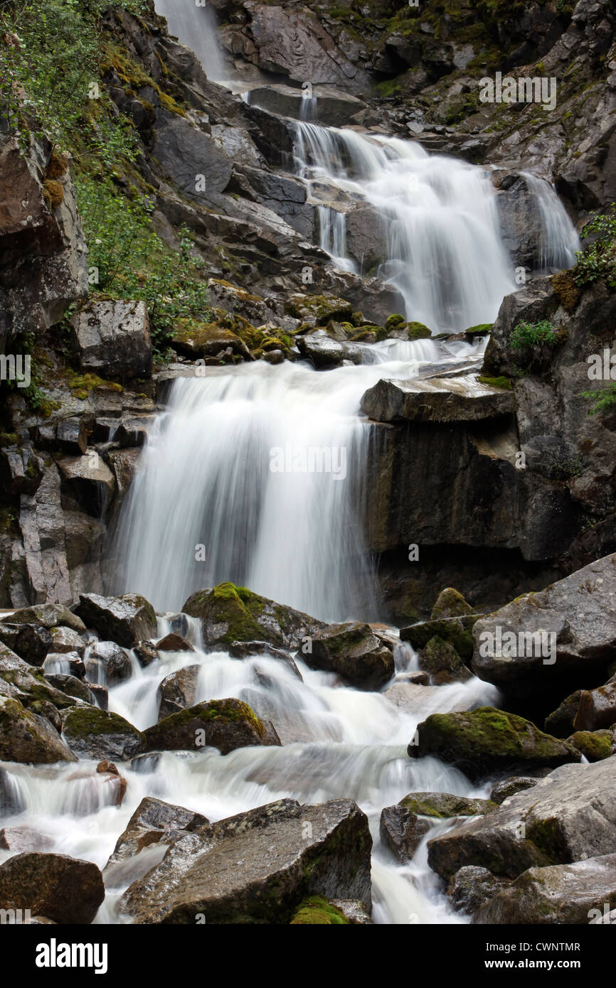 Waterfall cascading down a rocky mountain ravine with green ferns and ...