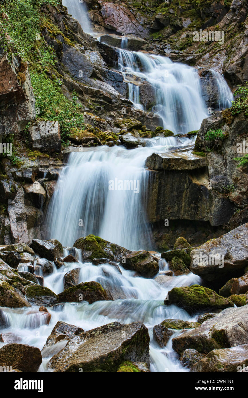 Waterfall cascading down a rocky mountain ravine with green ferns and ...