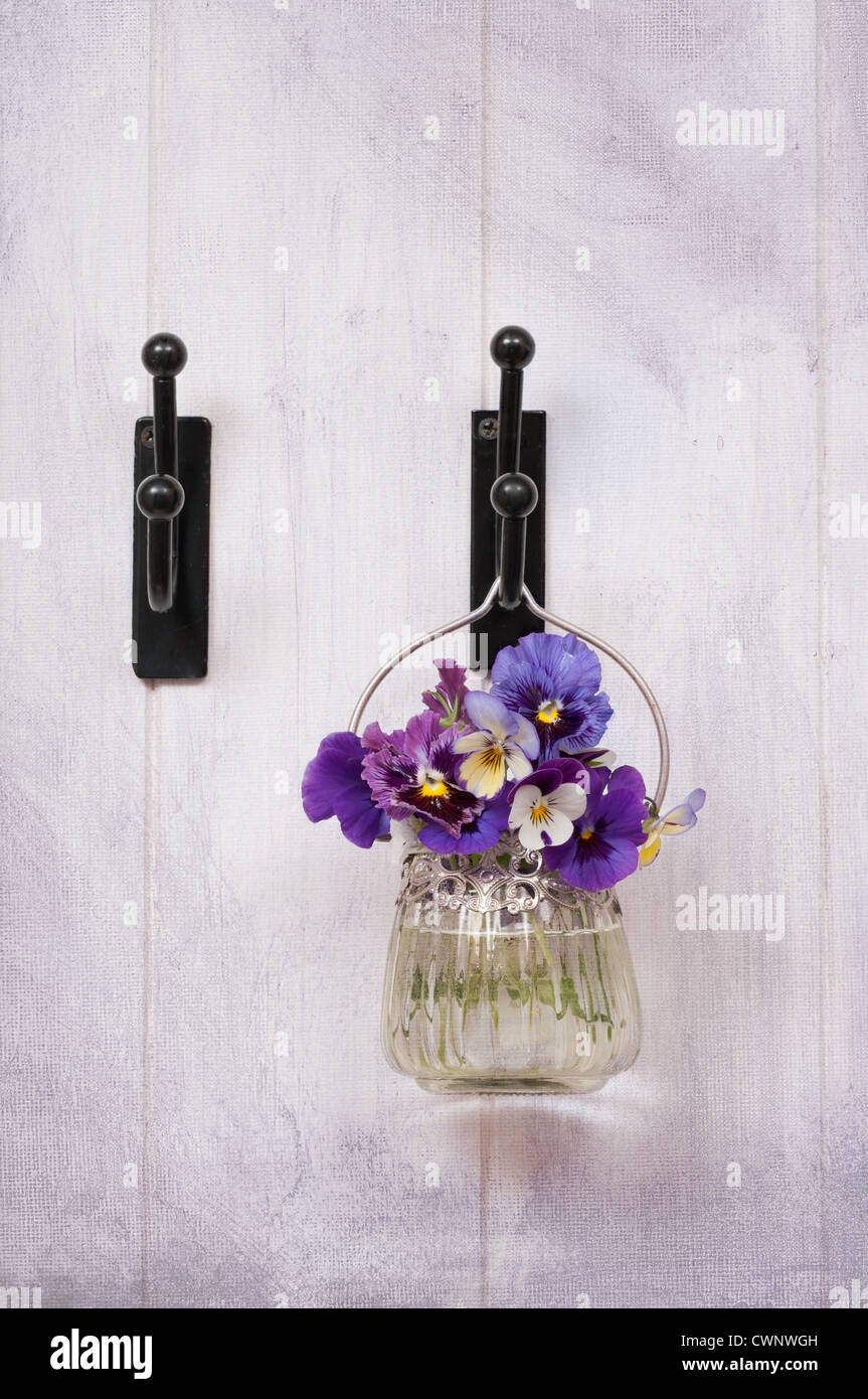 Glass vase of pansies hanging from hook with textured wooden background ...