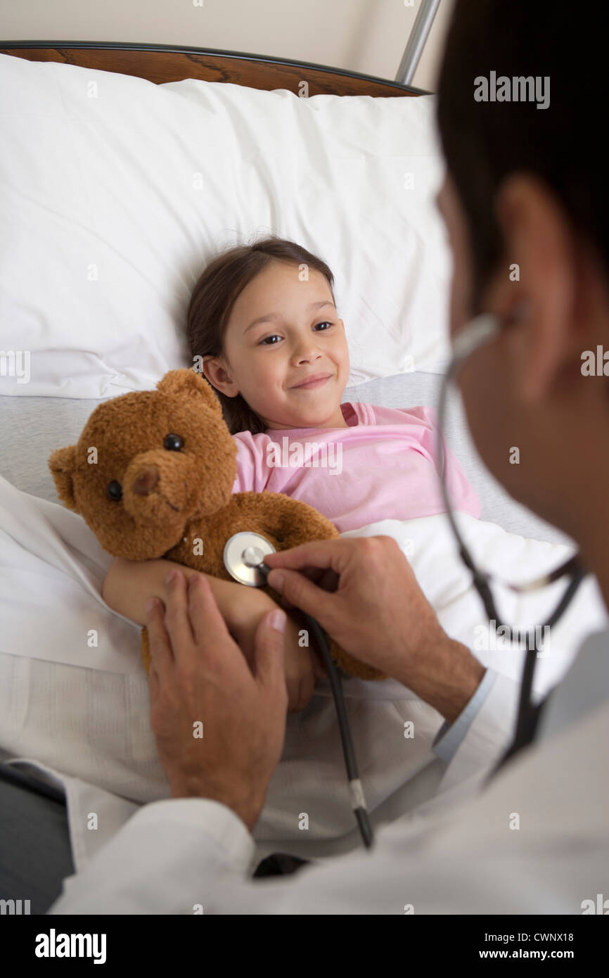 Doctor comforting young patient by examining her teddy bear with a ...