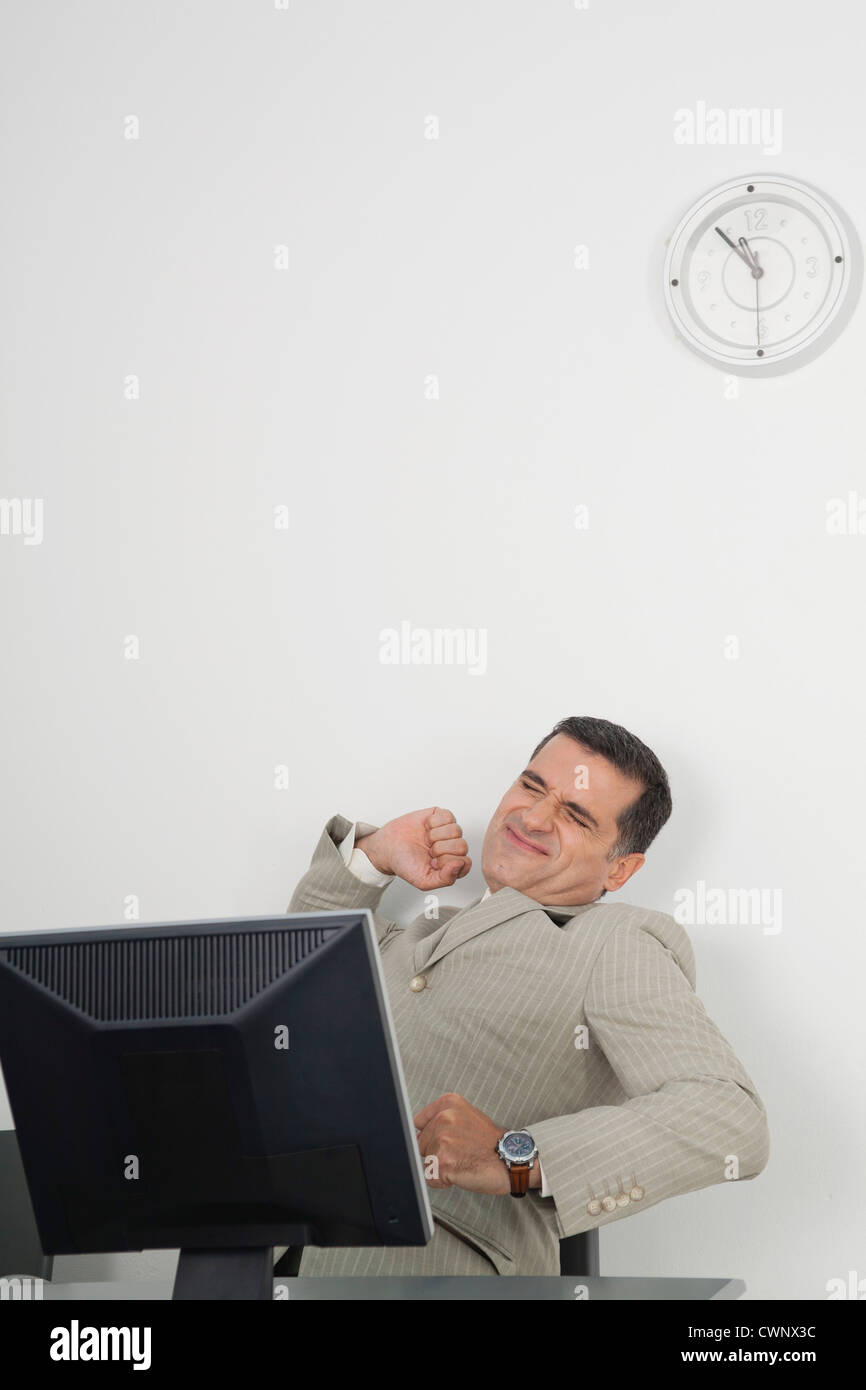 Mature businessman stretching at desk Stock Photo - Alamy