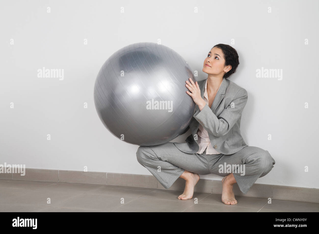 Young businesswoman crouching against wall holding fitness ball Stock ...